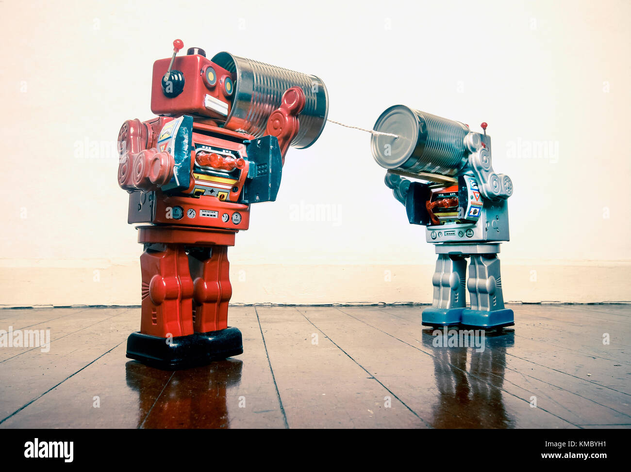 Two retro Robots toys talking on tin can phones on an old wooden floor ...