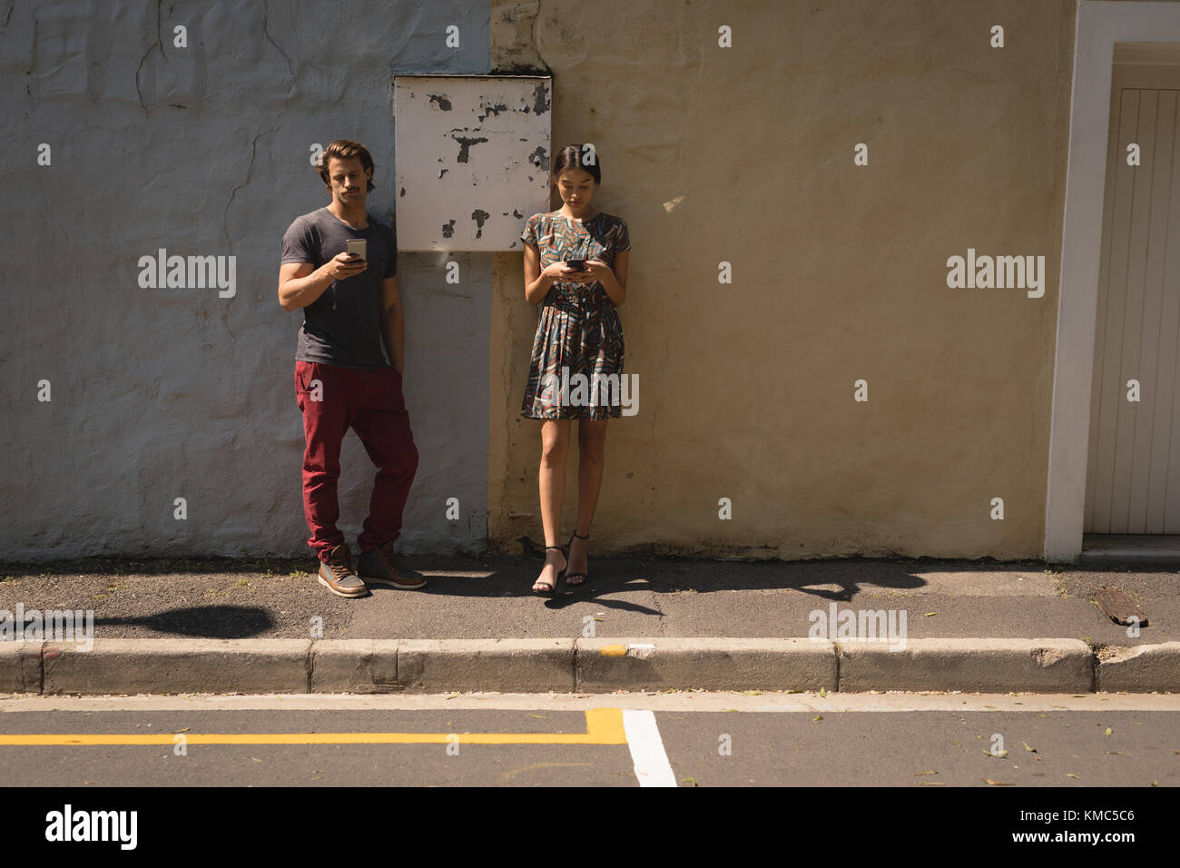 Couple using mobile phone against wall Stock Photo - Alamy