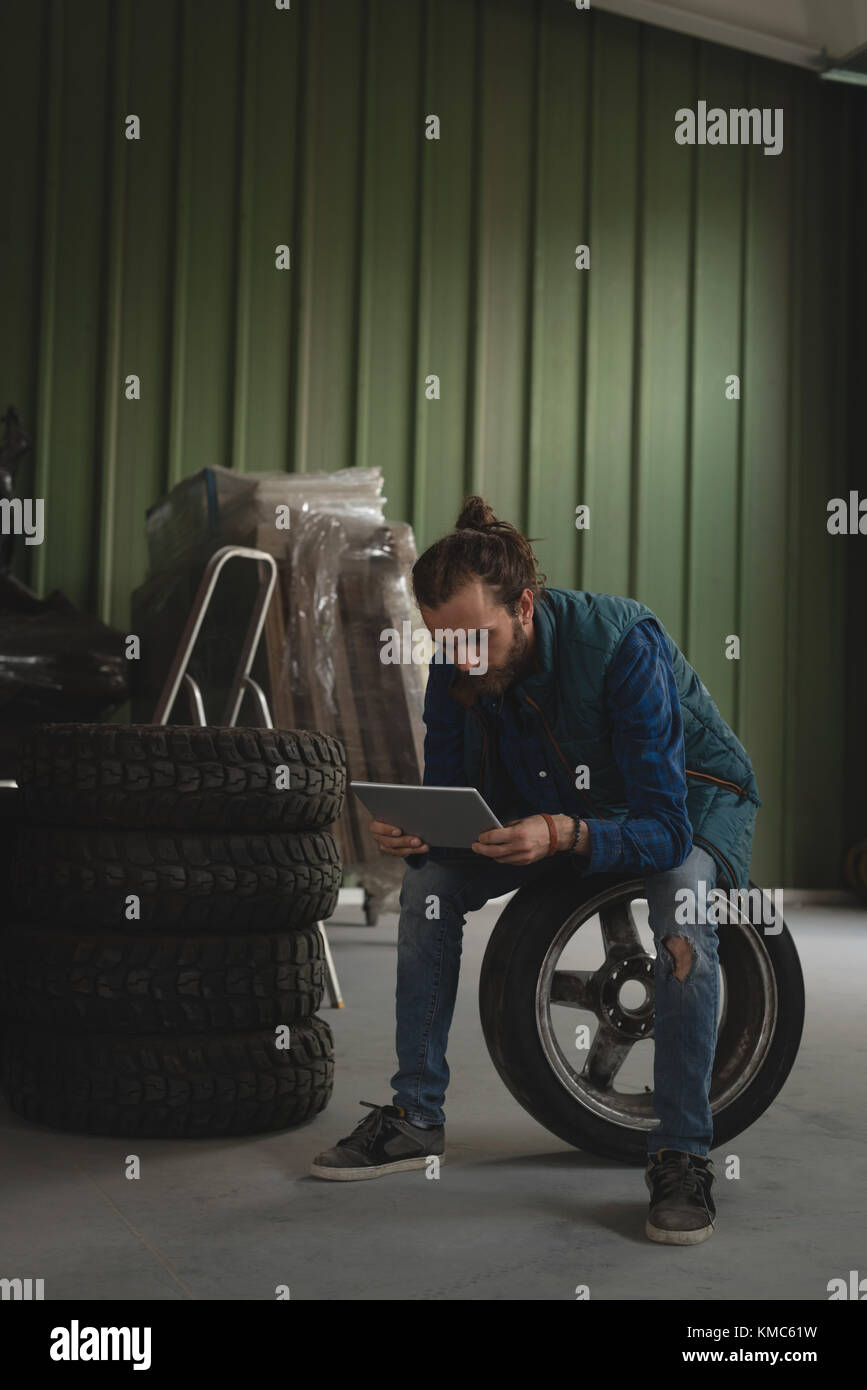Man sitting on tyre and using digital tablet Stock Photo - Alamy