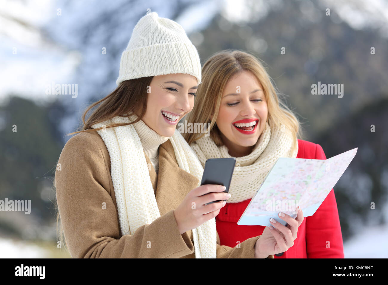 Two happy tourists reading a paper map in winter holidays in a snowy ...