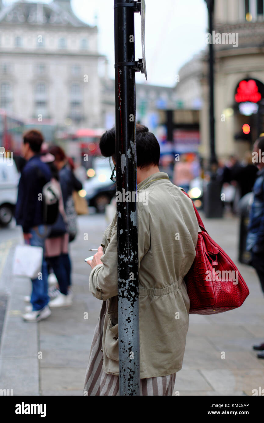 woman leaning against sign post and smoking a cigarette in London ...