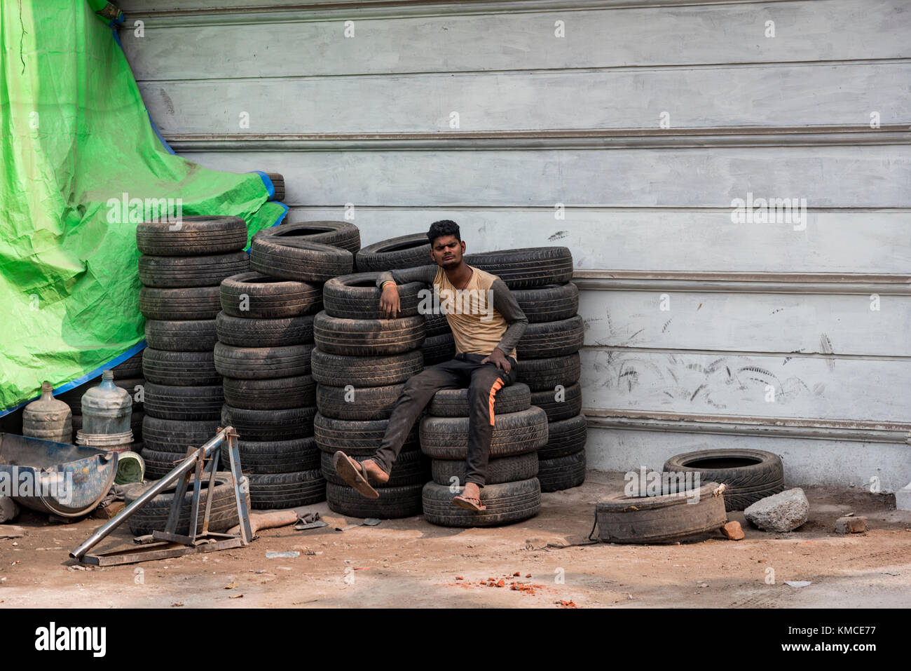 A man sitting and relaxing on a stack of tyres at his workshop Stock ...
