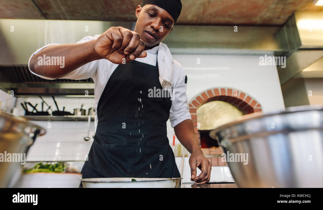 Chef sprinkling spices on dish in commercial kitchen. African male cook ...
