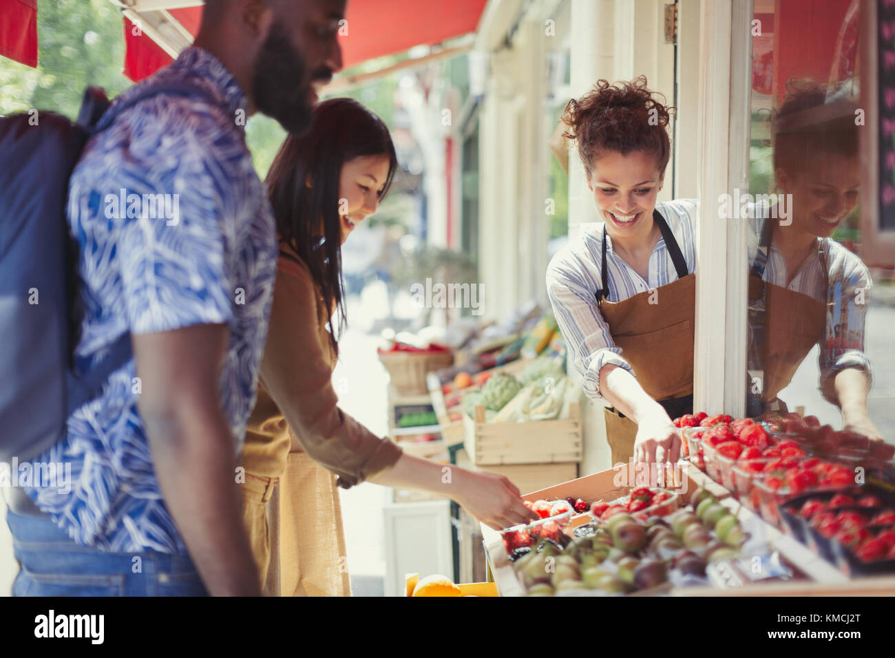 Worker helping couple shopping for fruit at storefront sidewalk Stock ...