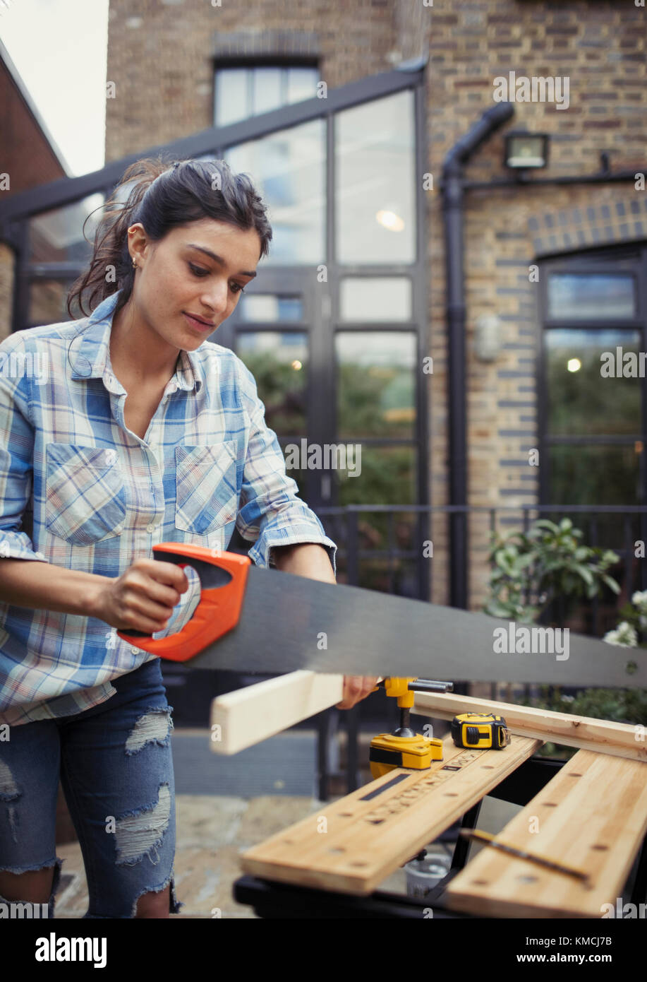 Young woman with saw cutting wood on patio Stock Photo - Alamy