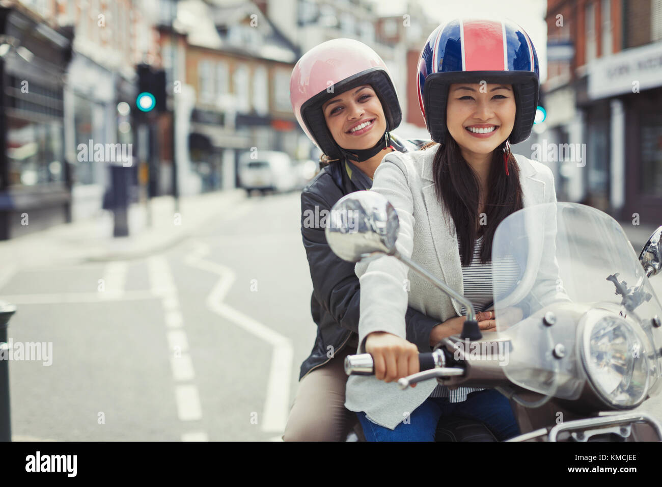 Smiling young women friends wearing helmets, riding motor scooter on ...