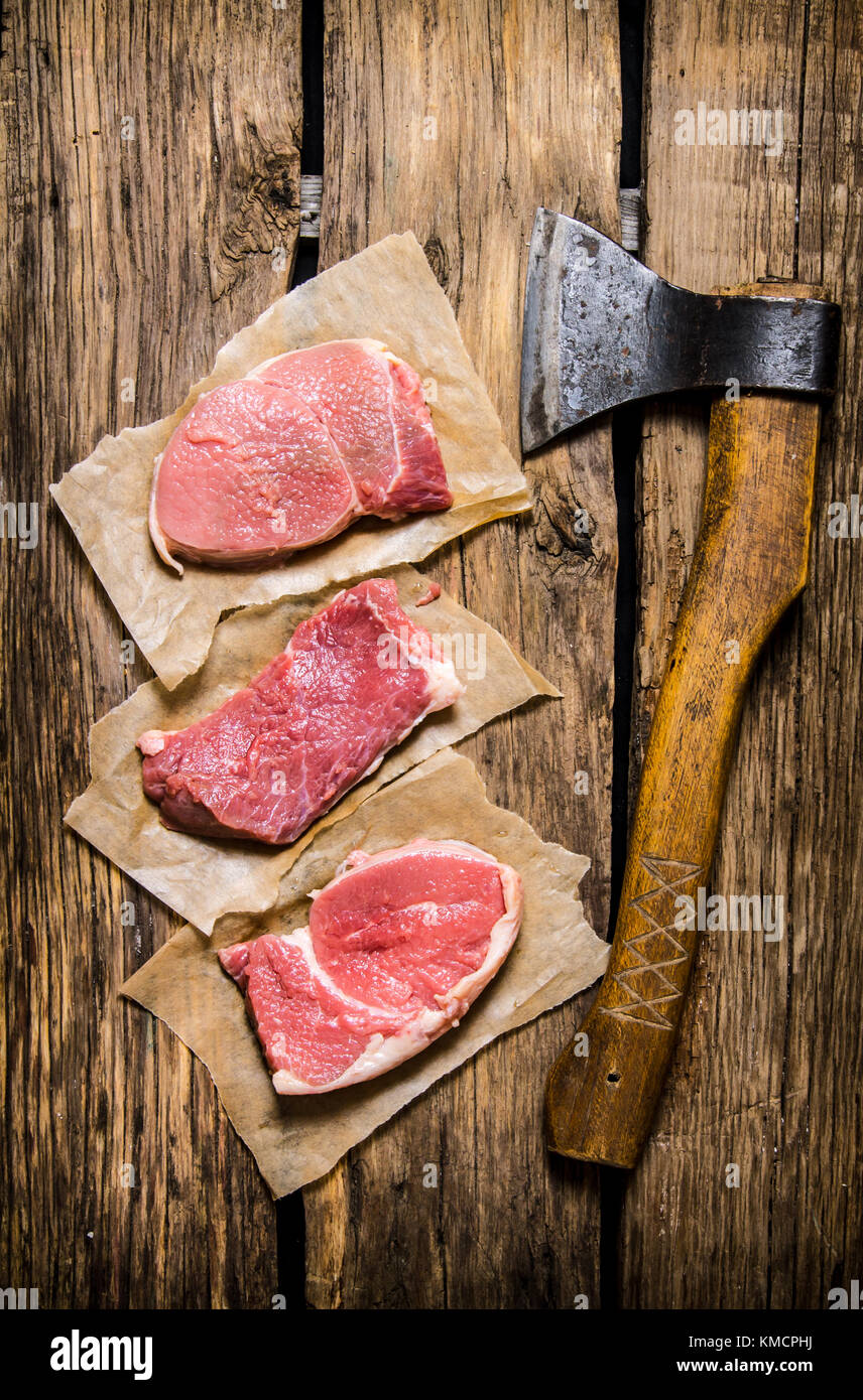 Medallions of raw meat on a tree with an axe. On wooden background. Top ...