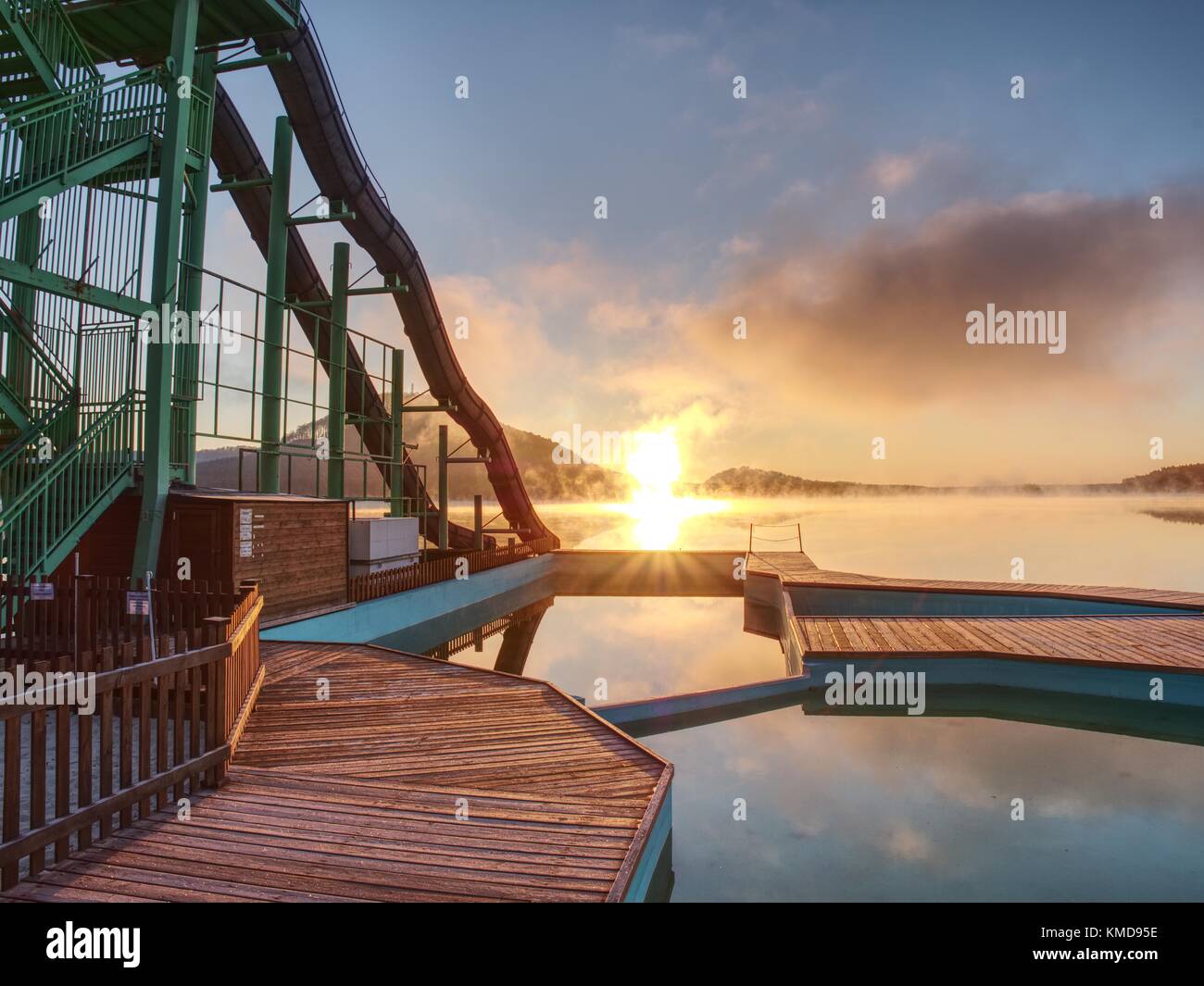 Sunset shore and toboggan slides at lake,. High ladder tower with ...