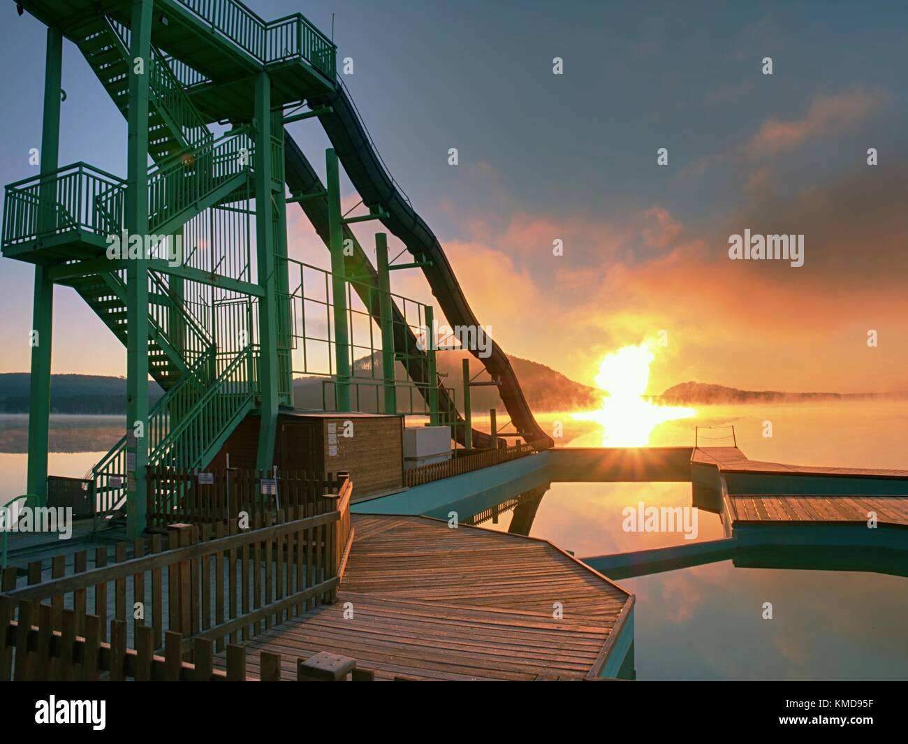 Sunset shore and toboggan slides at lake,. High ladder tower with ...