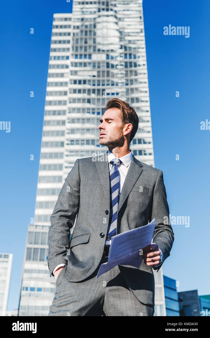businessman stands in front of a skyscraper and is angry while reading ...