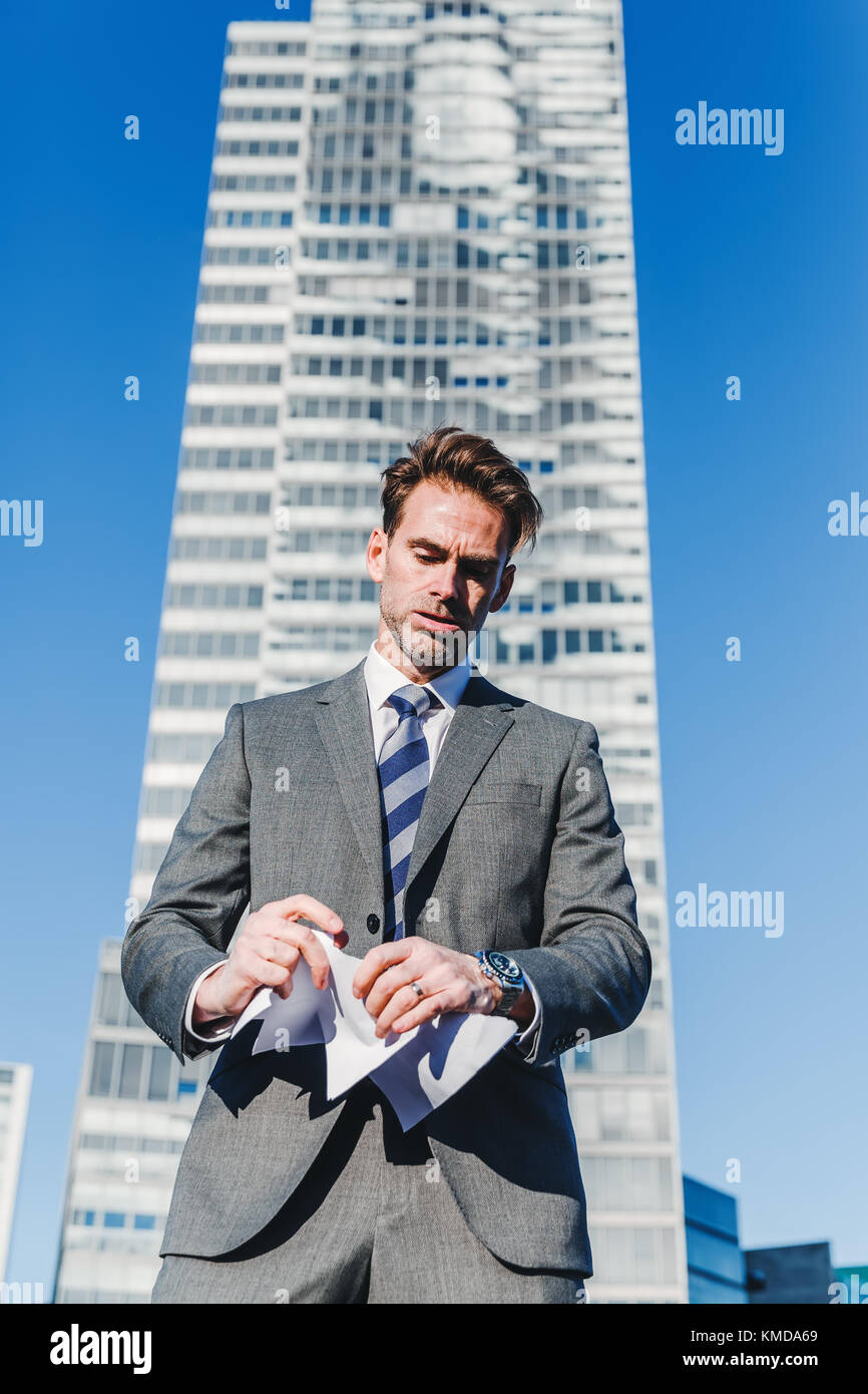 angry businessman stands in front of a skyscraper and rips documents in ...