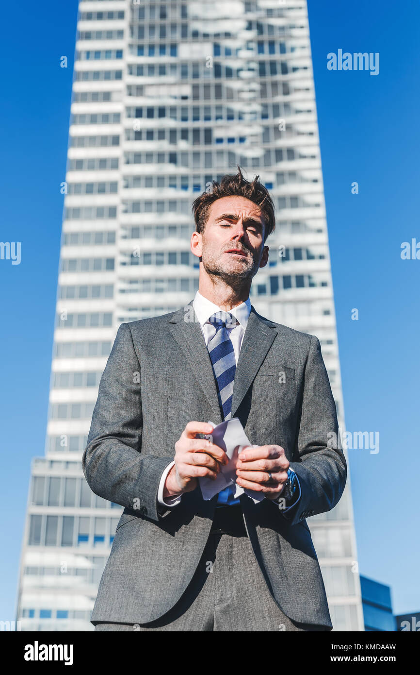 angry businessman stands in front of a skyscraper and rips documents in ...