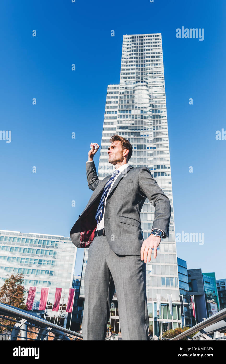 angry businessman stands in front of a skyscraper and crumples up ...