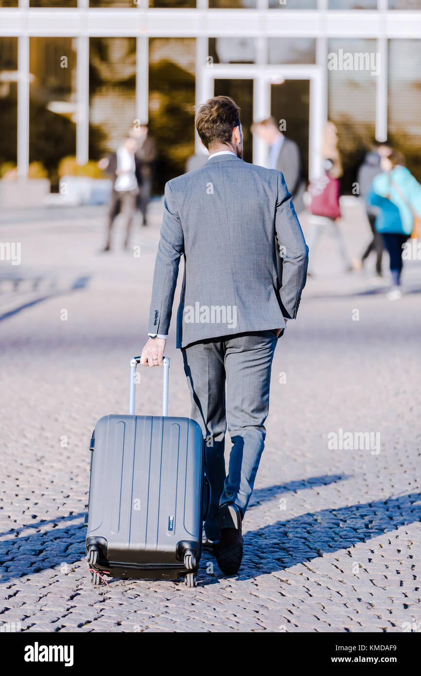 rear view of a businessman who walks with a trolley bag in the city ...