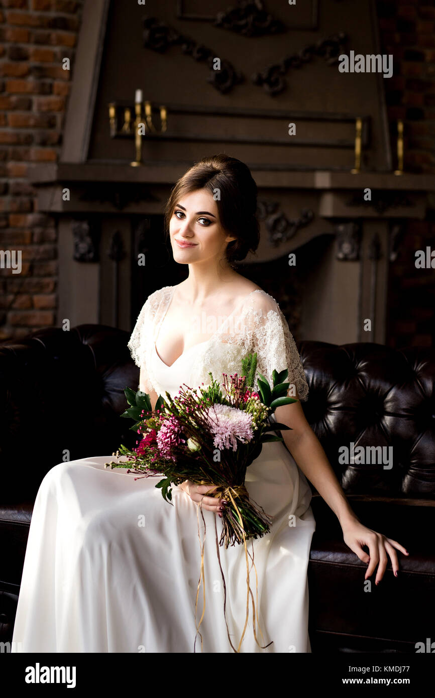 Bride in beautiful dress sitting on chair indoors in dark studio ...