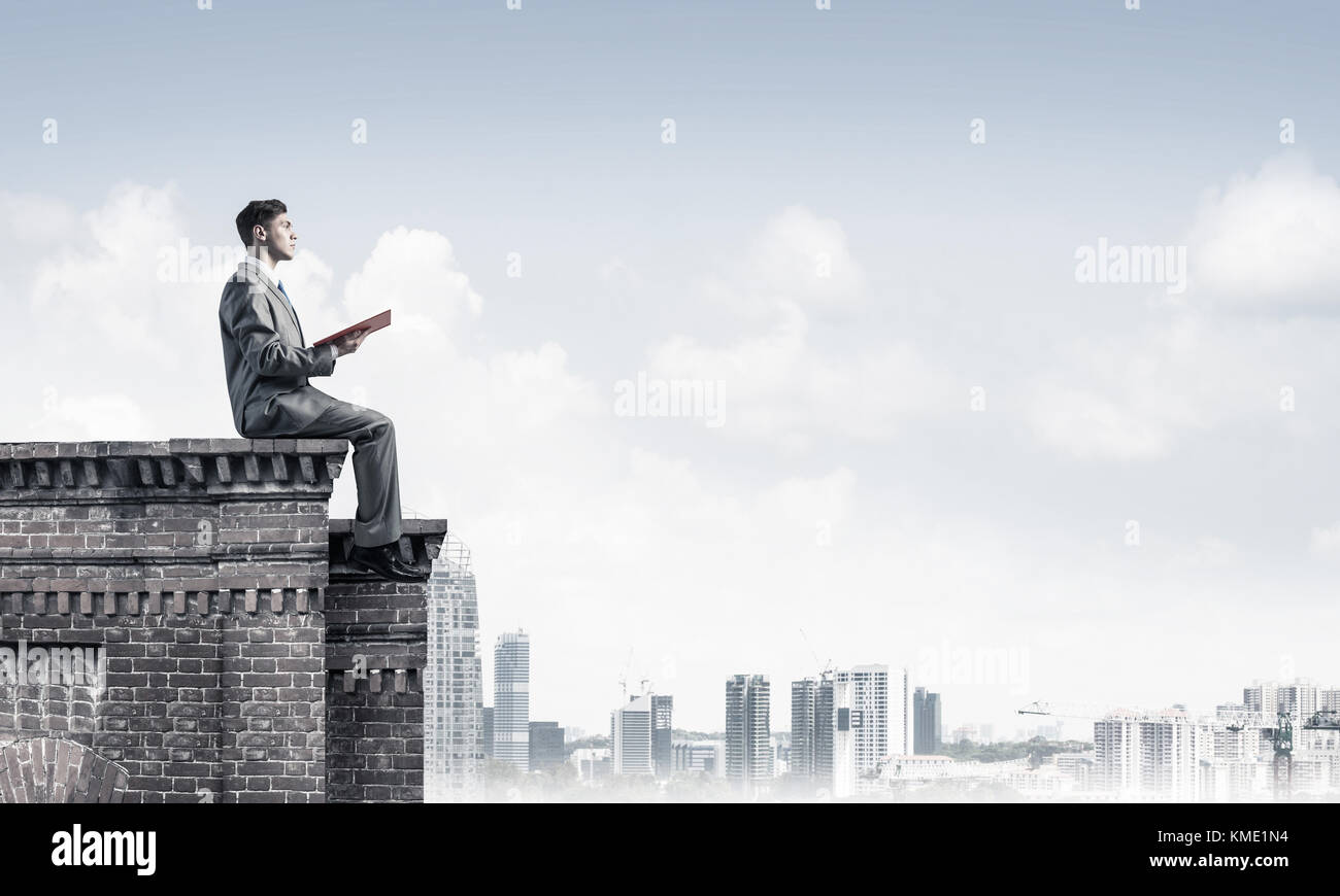 Man on roof edge reading book and cityscape at background Stock Photo ...