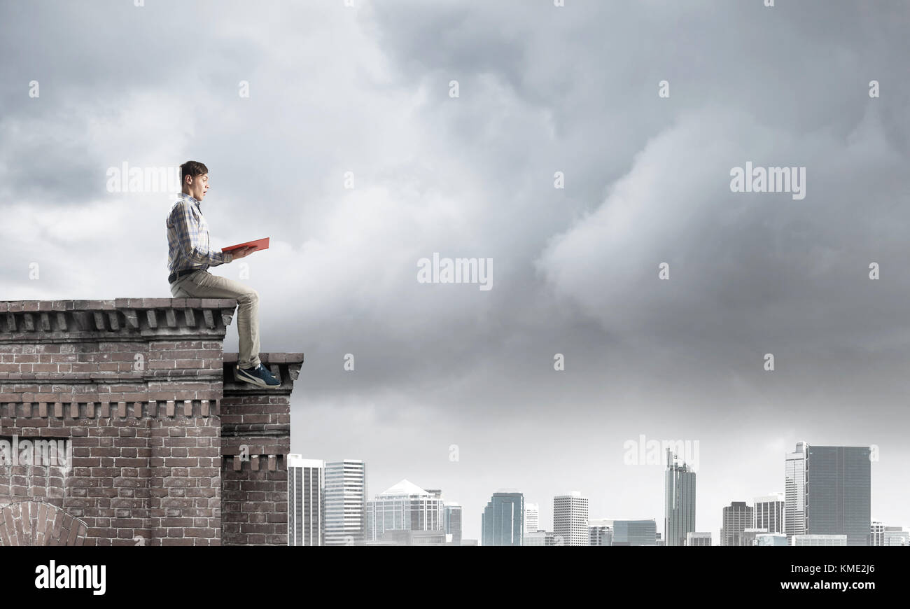 Man on roof edge reading book and cityscape at background Stock Photo ...