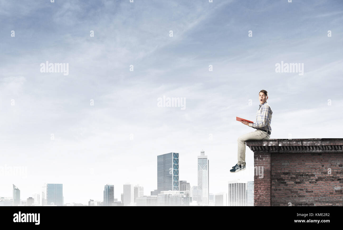 Man on roof edge reading book and cityscape at background Stock Photo ...