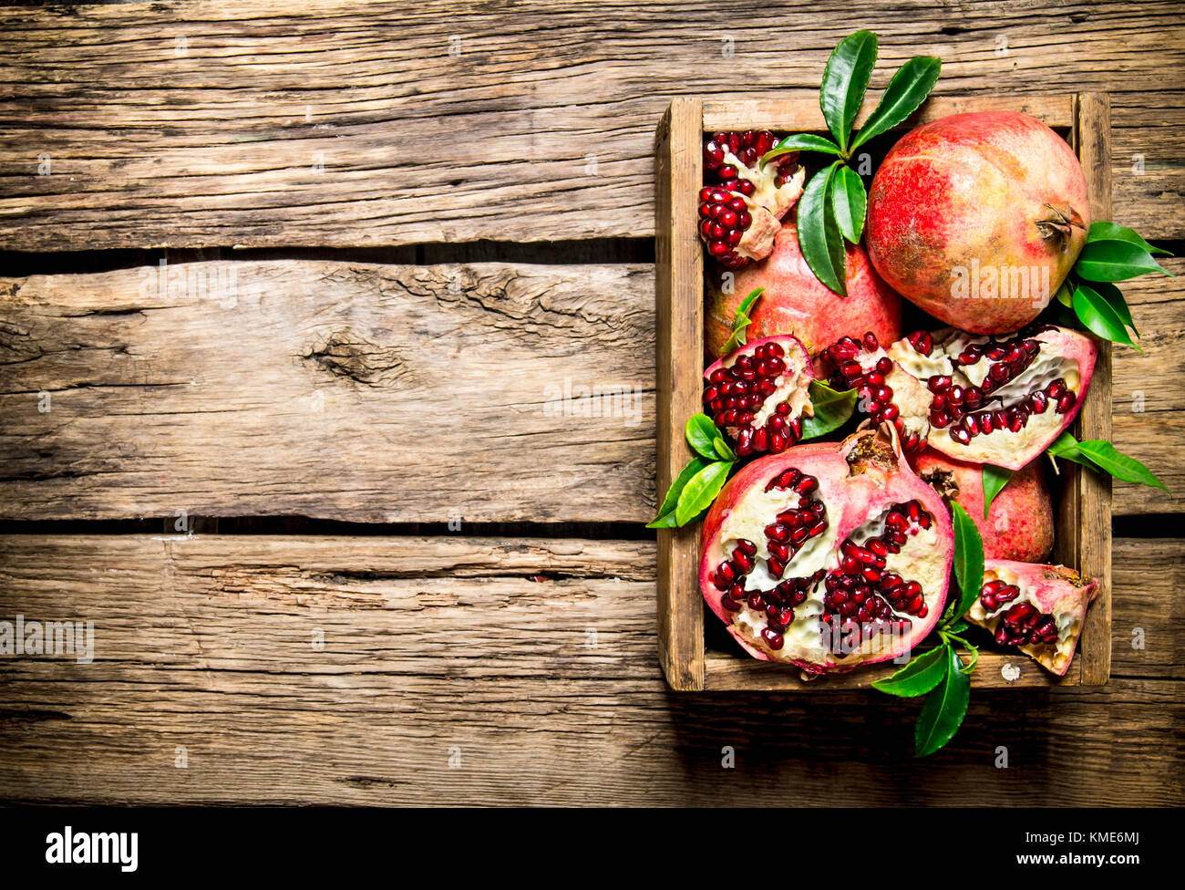 Fresh pomegranates in an old box with leaves. On wooden background ...