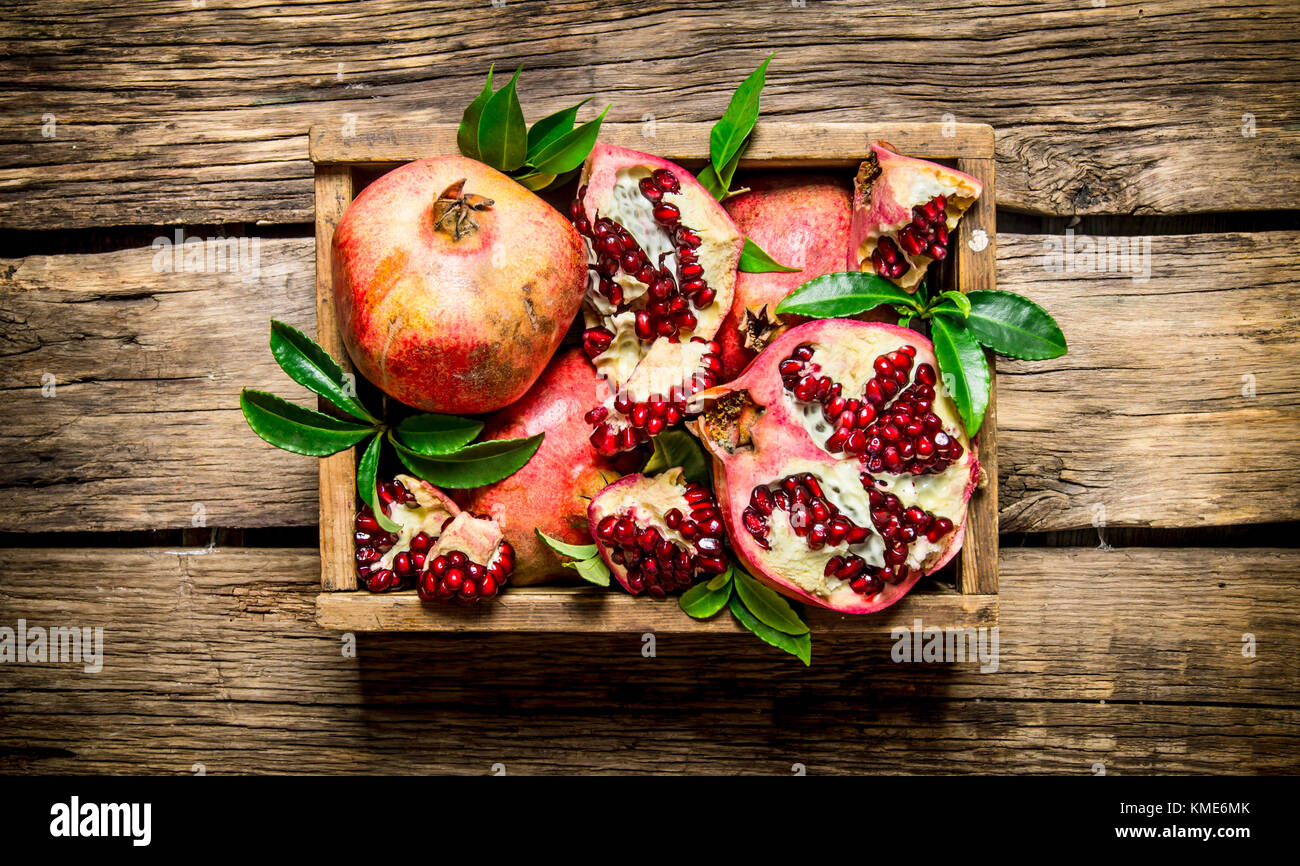 Fresh pomegranates in an old box with leaves. On wooden background. Top ...