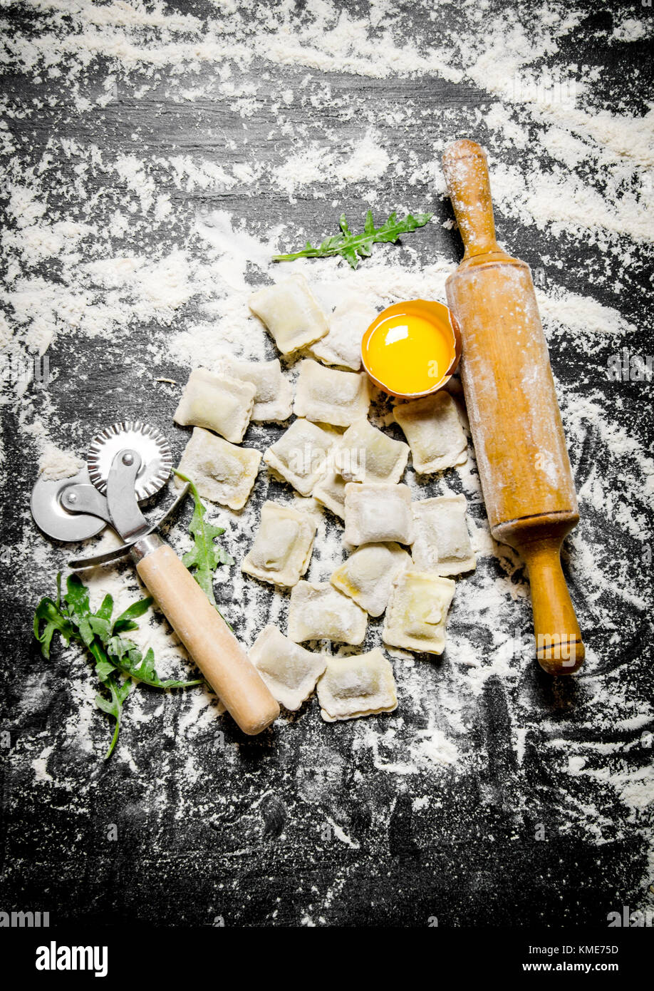 Homemade fresh ravioli with egg, a rolling pin and knife. On the black ...