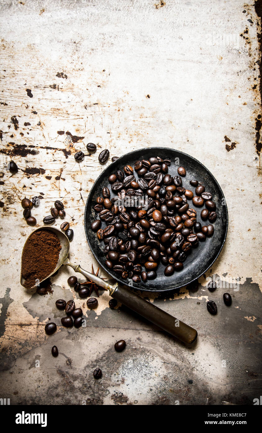 Roasted coffee beans in a pan with a spoonful of ground. On rustic ...