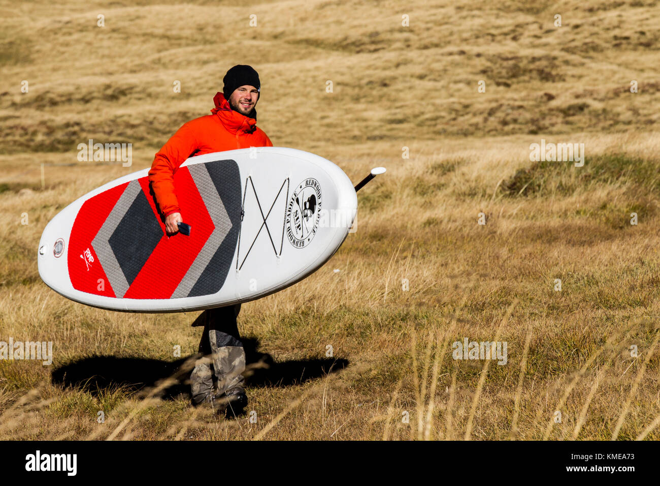 Stand up paddle boarder standing in meadow,looking at camera and ...