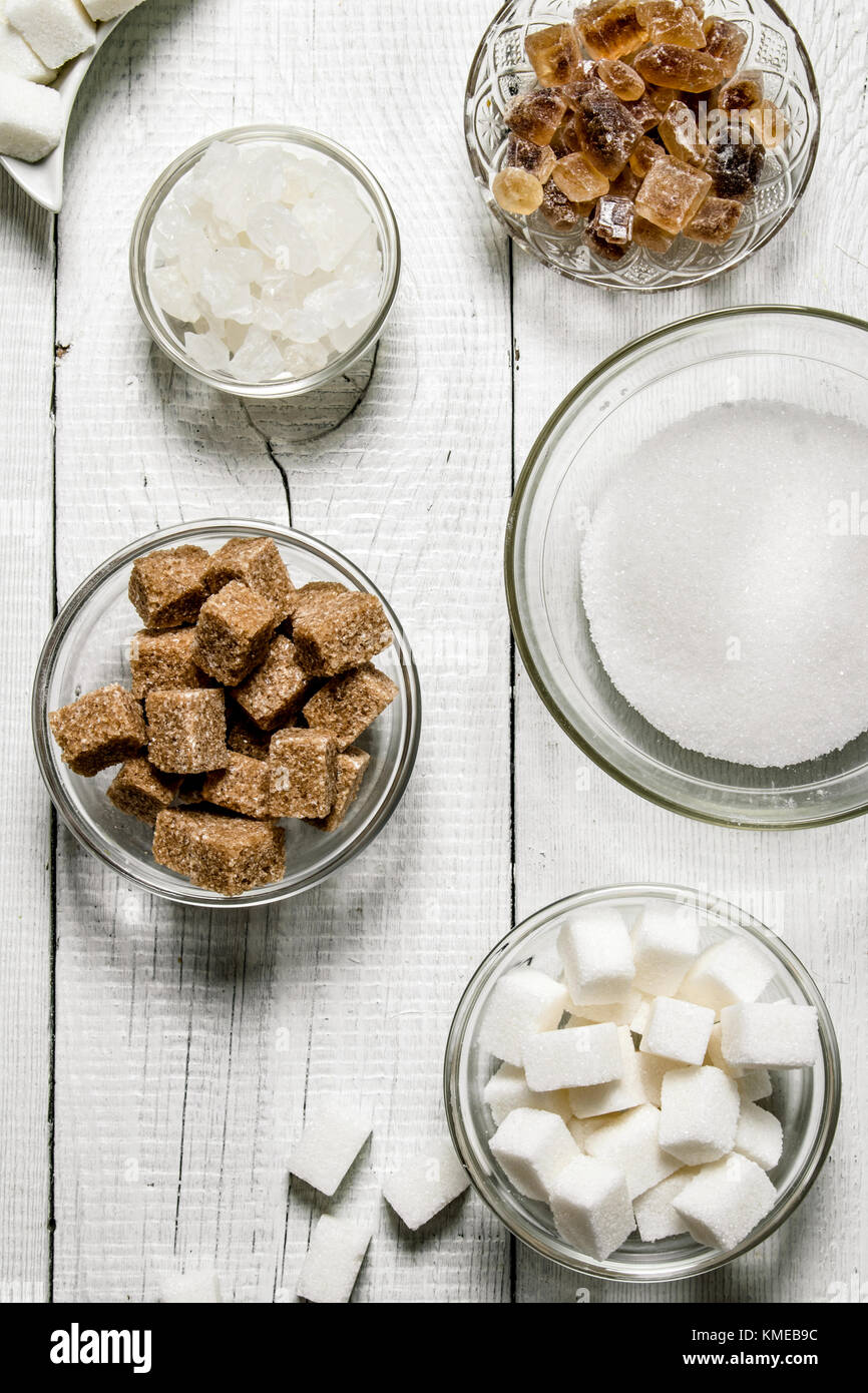 Different types of brown and white sugar in the cups. On a white wooden ...