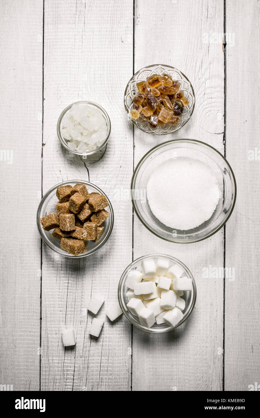 Different types of brown and white sugar in the cups. On a white wooden ...