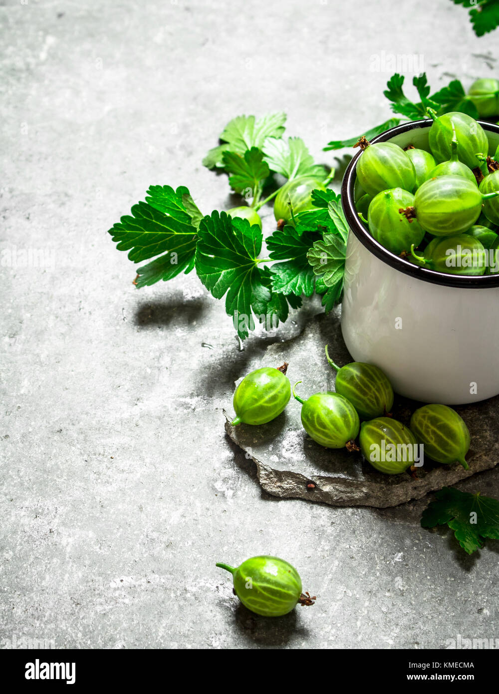 Gooseberries and leaves in a mug. On the stone table Stock Photo - Alamy