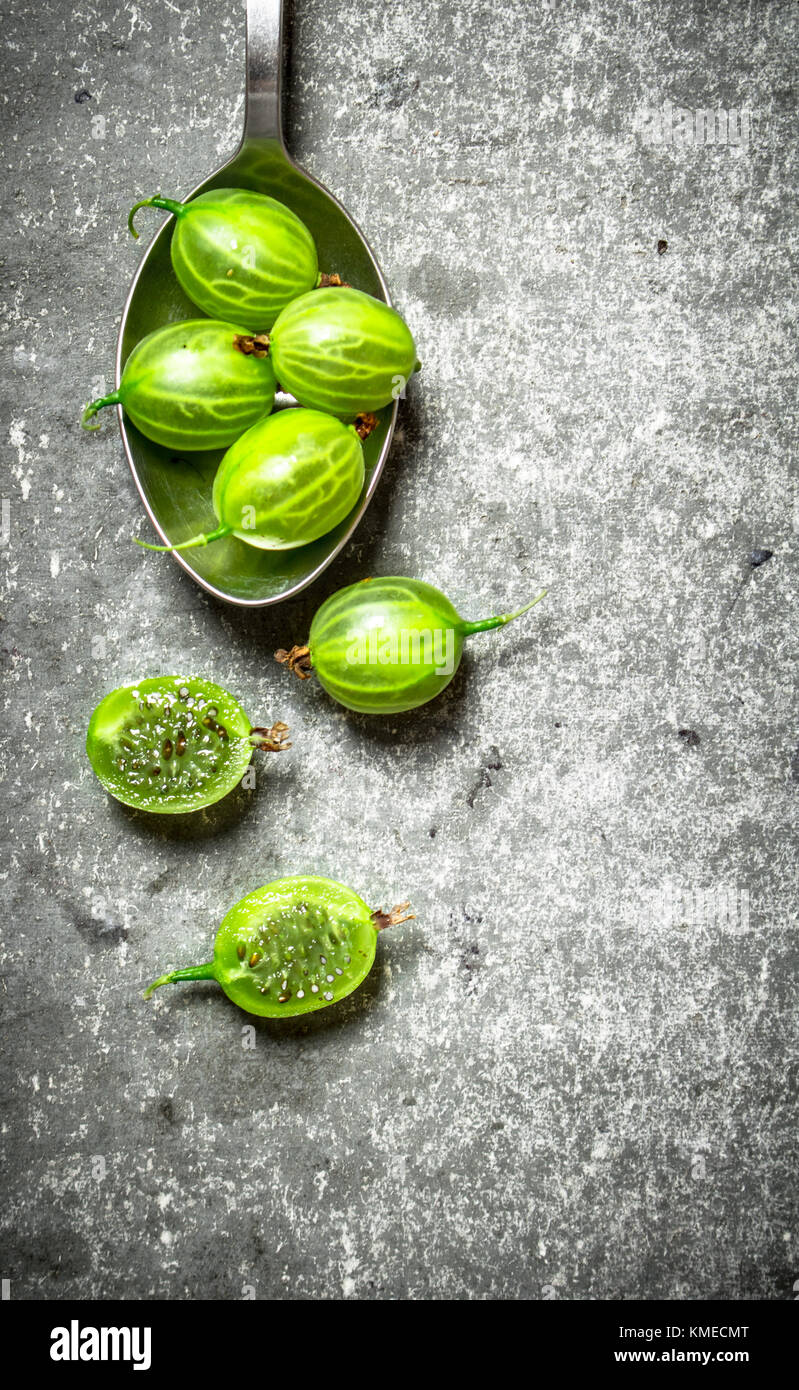 Green gooseberry in a spoon. On a stone background Stock Photo - Alamy