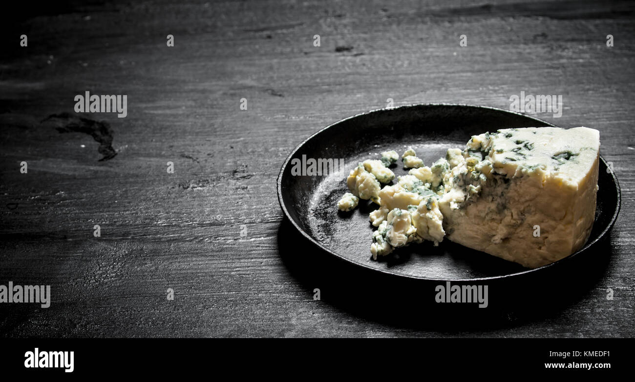 Aromatic cheese with blue mold on an old plate. On a black wooden ...