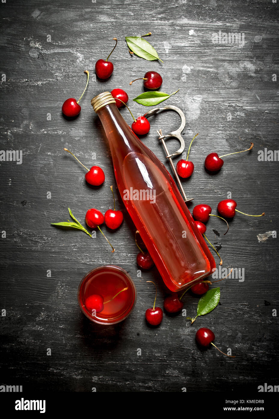 bottle of fresh cherry juice with the leaves around. On a black wooden ...
