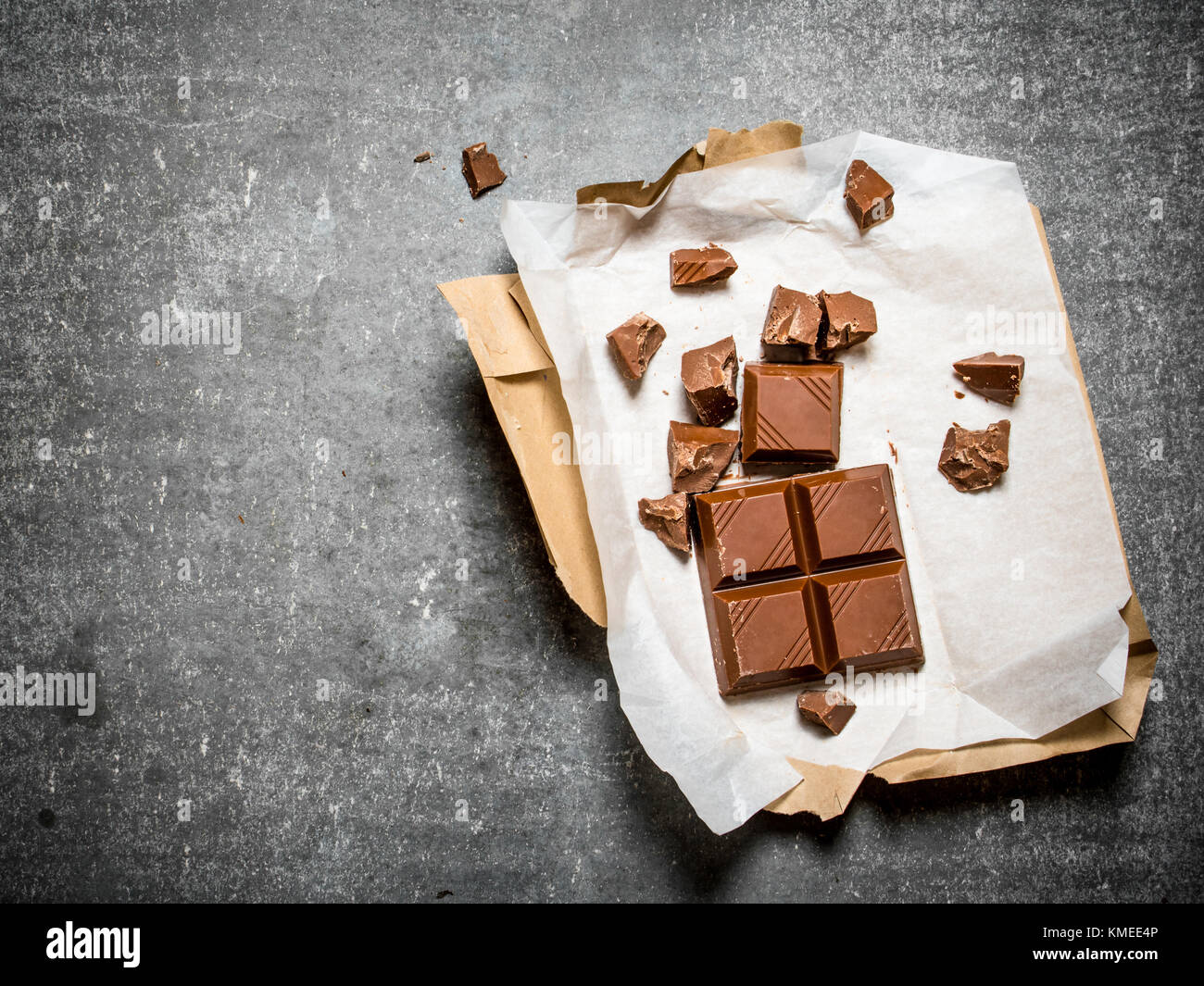 Milk chocolate in paper. On the stone table Stock Photo - Alamy