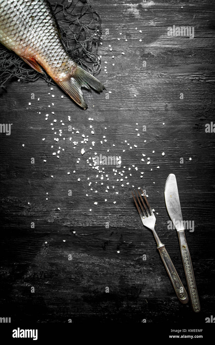 Raw fish with a knife and fork. On a black wooden background Stock ...