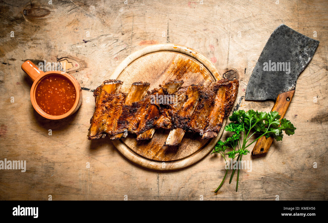 Barbecued ribs with tomato sauce and a carving hatchet. On wooden ...