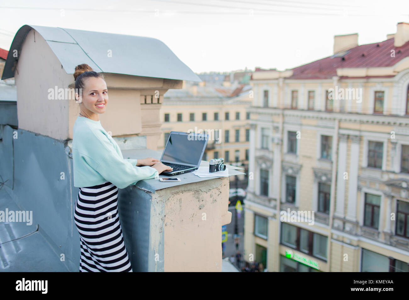 Beautiful and stylish girl works for a laptop on the roof of the house ...