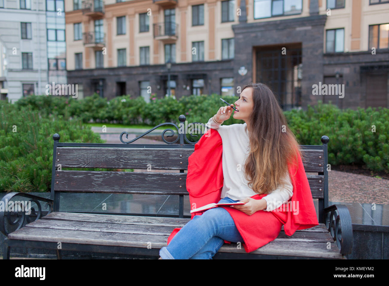 An attractive girl with long brown hair sits on a bench, hiding behind ...