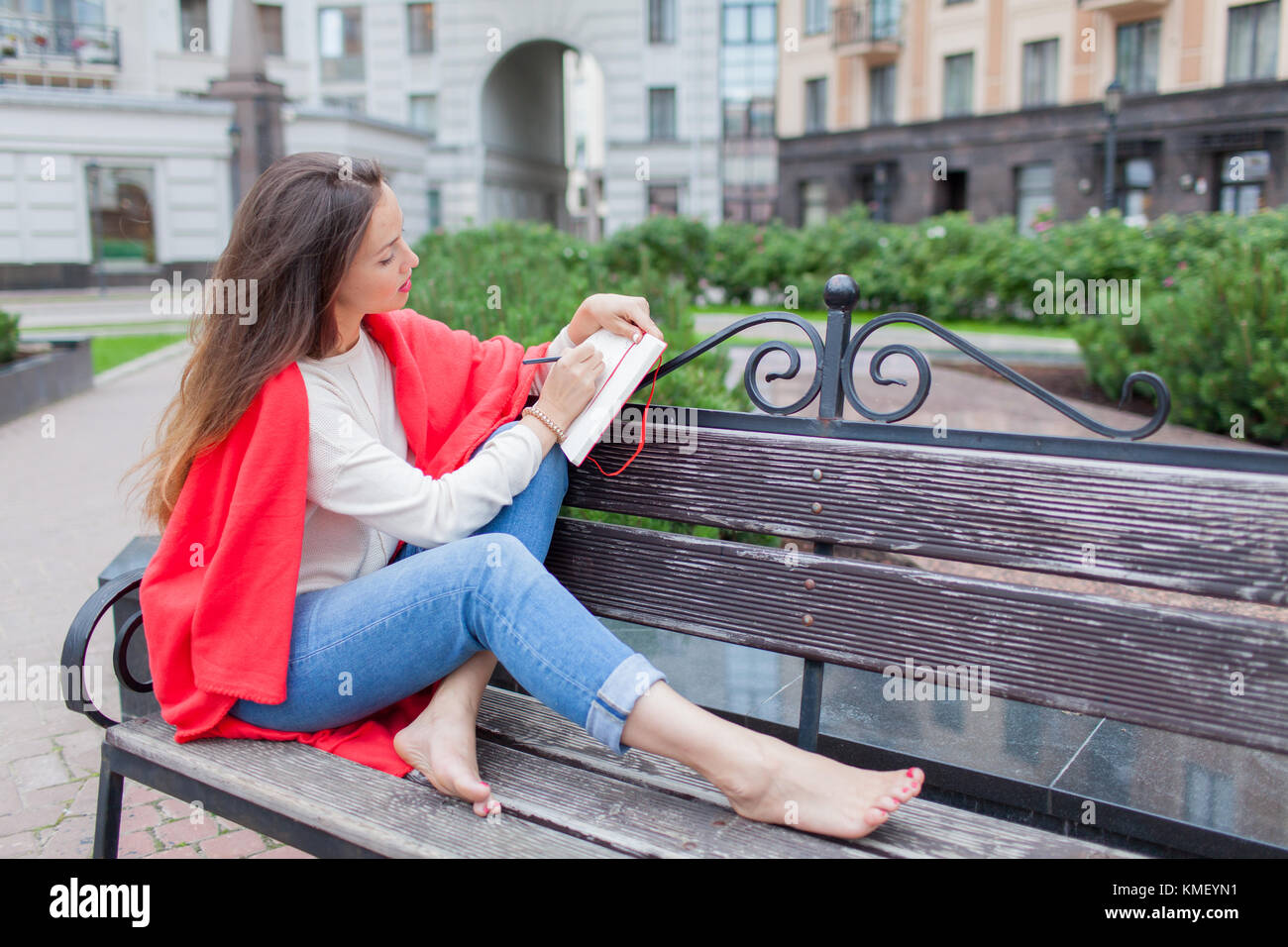 Attractive girl sitting on a bench with bare feet, covered with a red ...