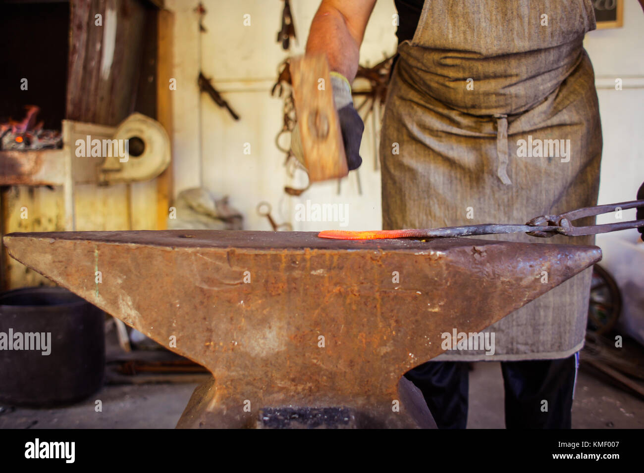 A blacksmith is hitting a piece of hot metal with the hammer on the ...