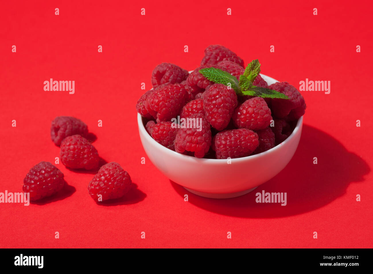 Bowl with fresh raspberries and mint leaves on a red background ...