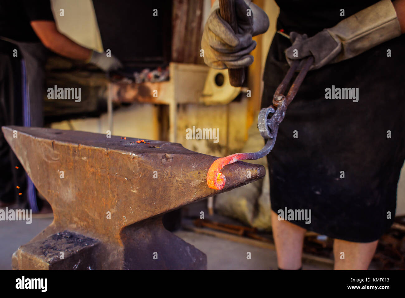 A blacksmith is hitting a piece of hot metal with the hammer on the ...