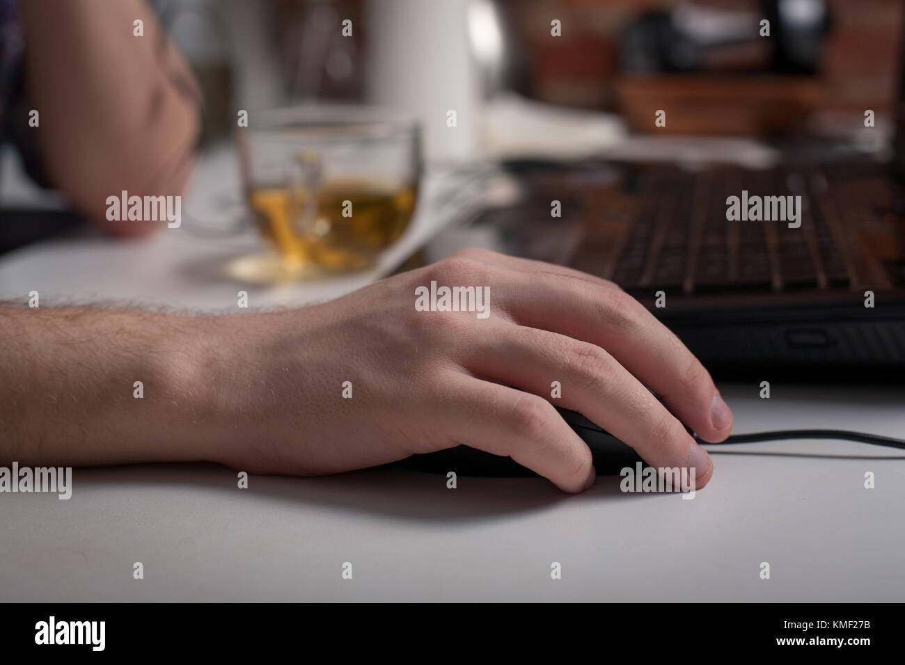 Male hand holding computer mouse with laptop keyboard in the background ...