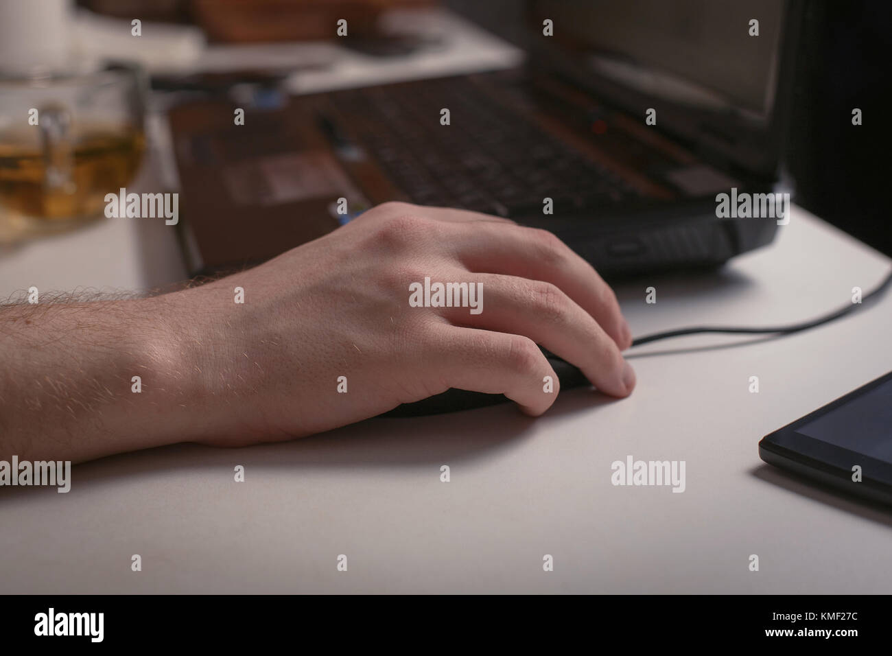 Male hand holding computer mouse with laptop keyboard in the background ...