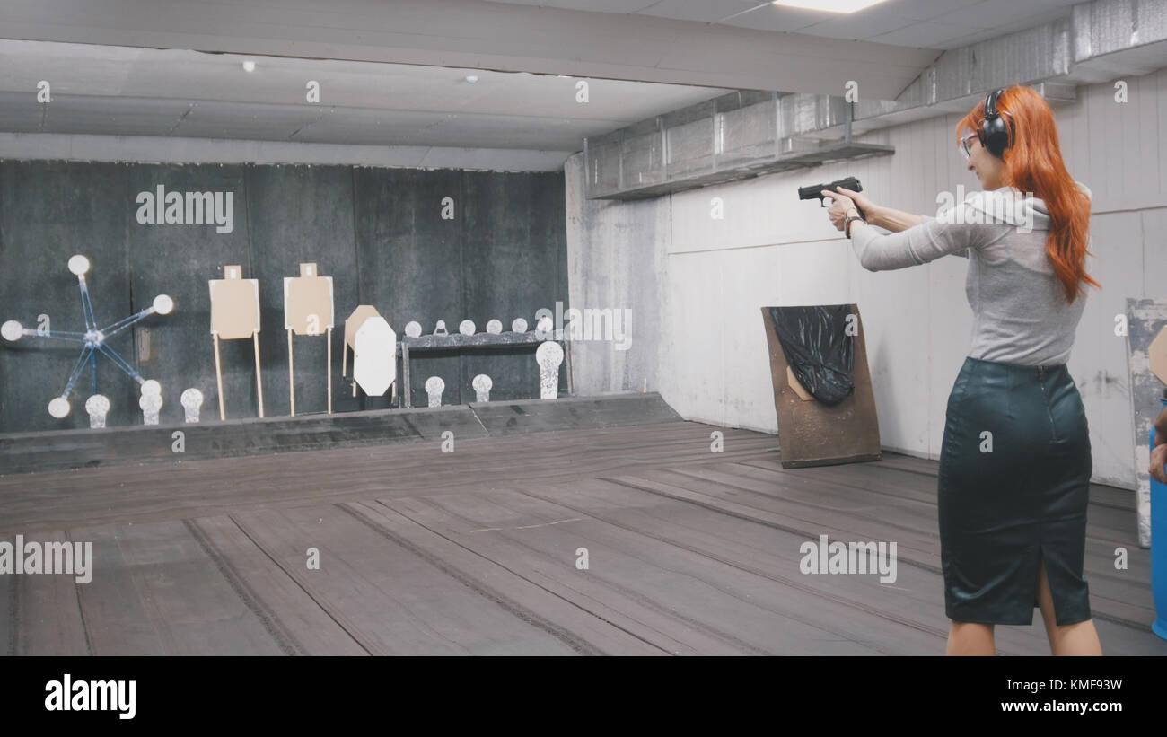 Woman with red hair shooting with a gun in shooting gallery Stock Photo ...