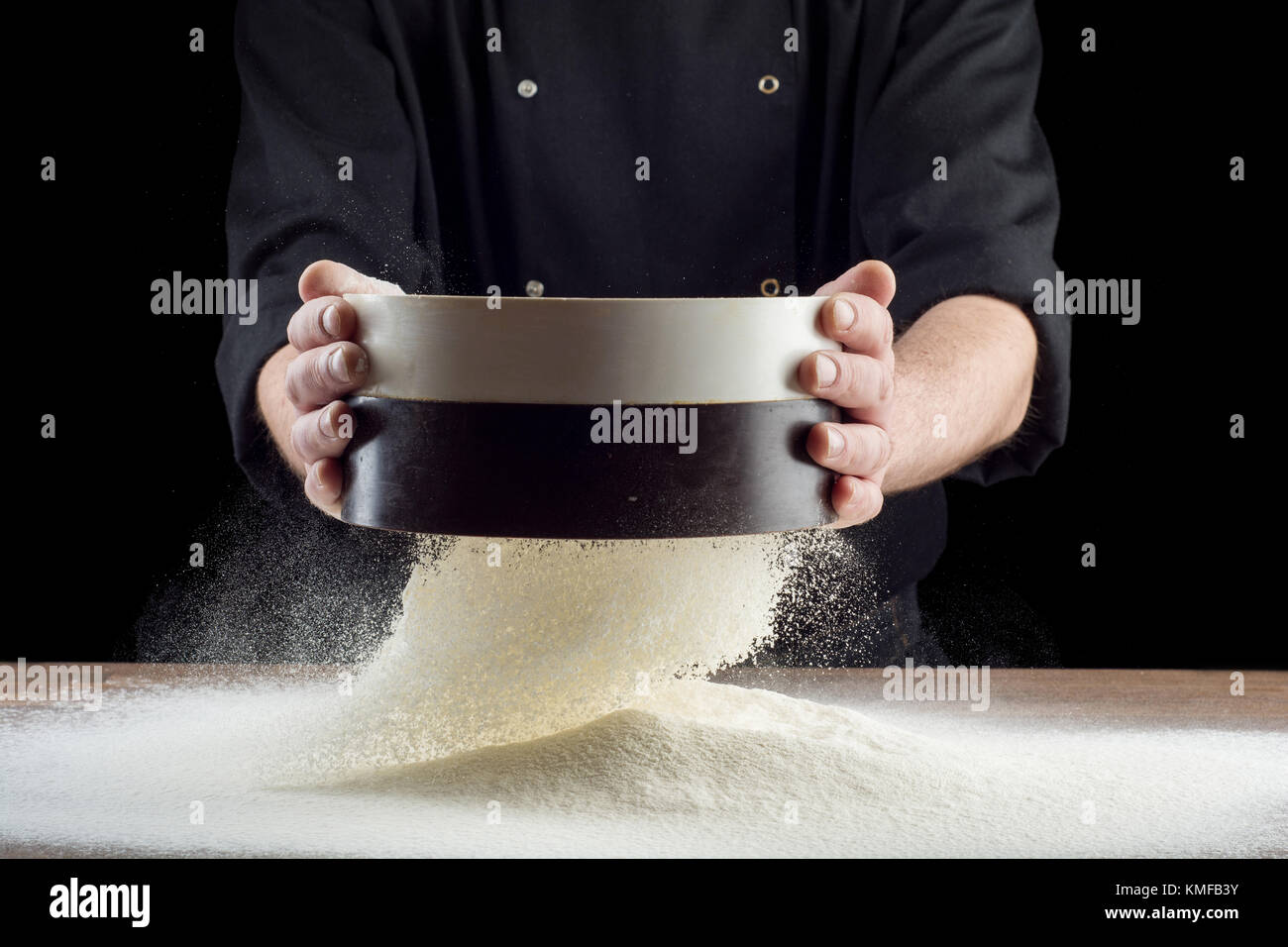 Male hands sifting flour from old sieve on old wooden kitchen table ...