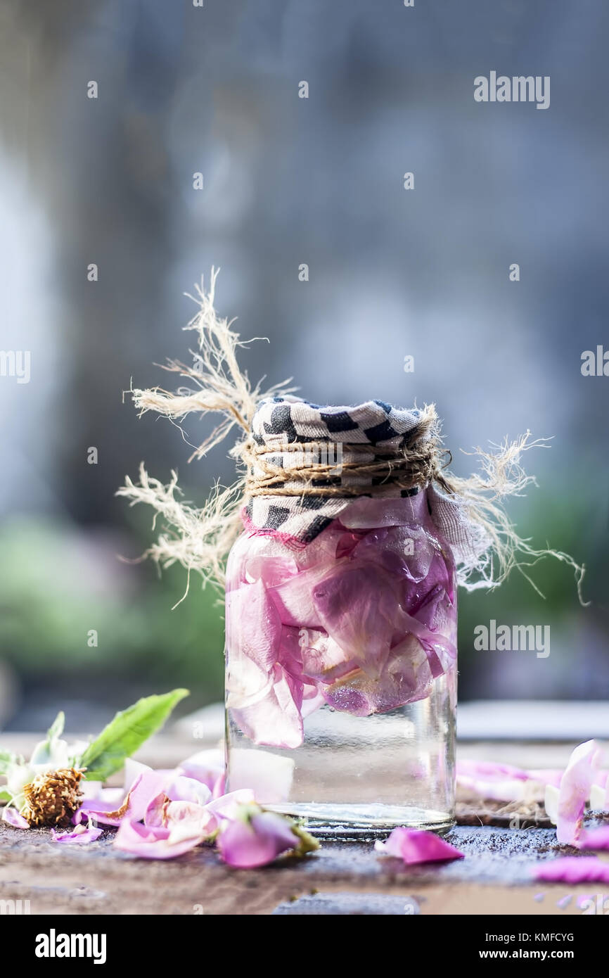 A transparent bottle contains rose water with rose petals in it.Concept ...