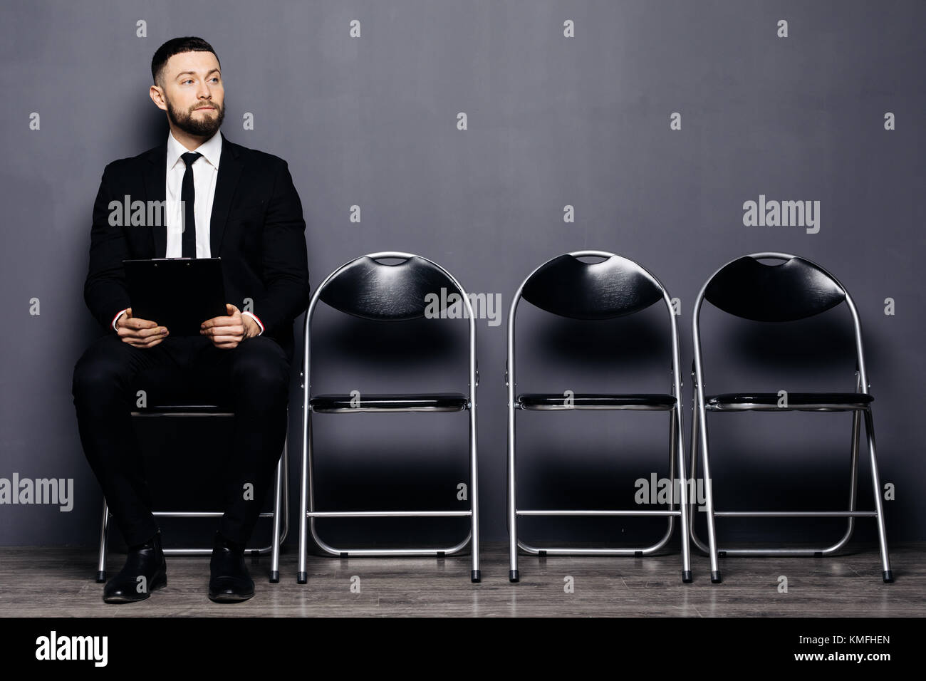 Confident job applicant reads resume while sitting on chair in row in ...