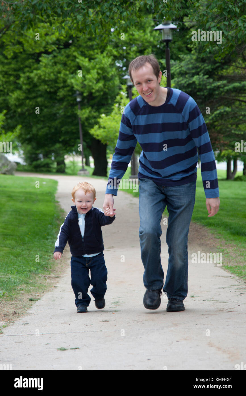 little boy holding his father's hand and walking together on a path in ...