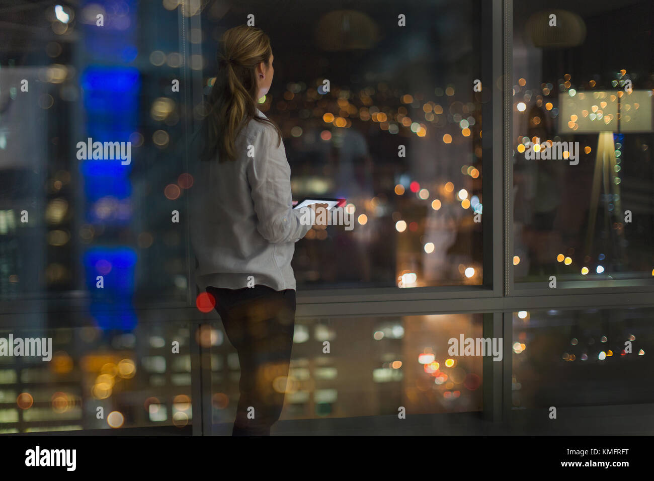 Pensive businesswoman with digital tablet working late, looking out ...